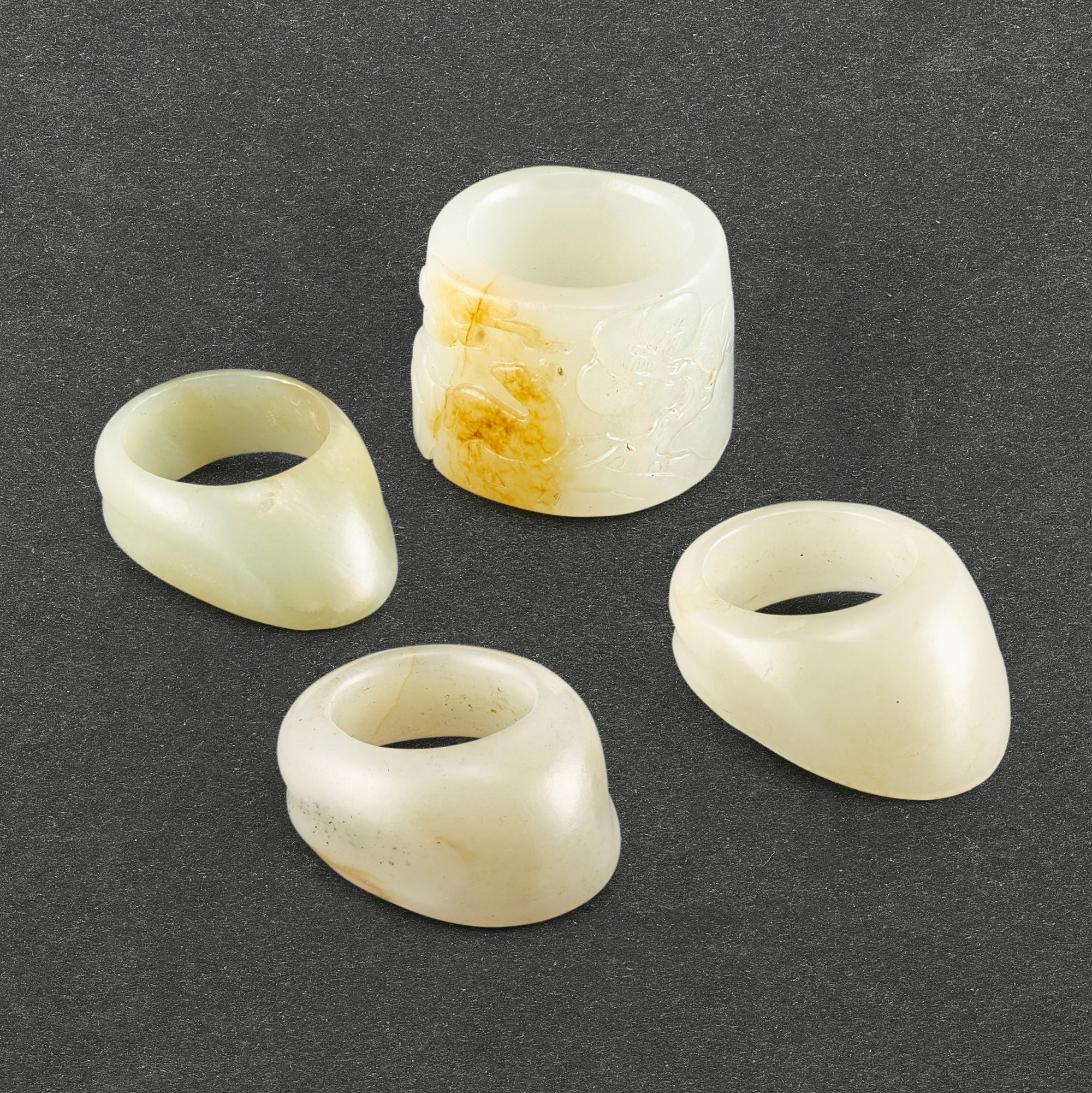 A WHITE AND RUSSET JADE 'PINE AND DEER' THUMB RING AND THREE CELADON ...