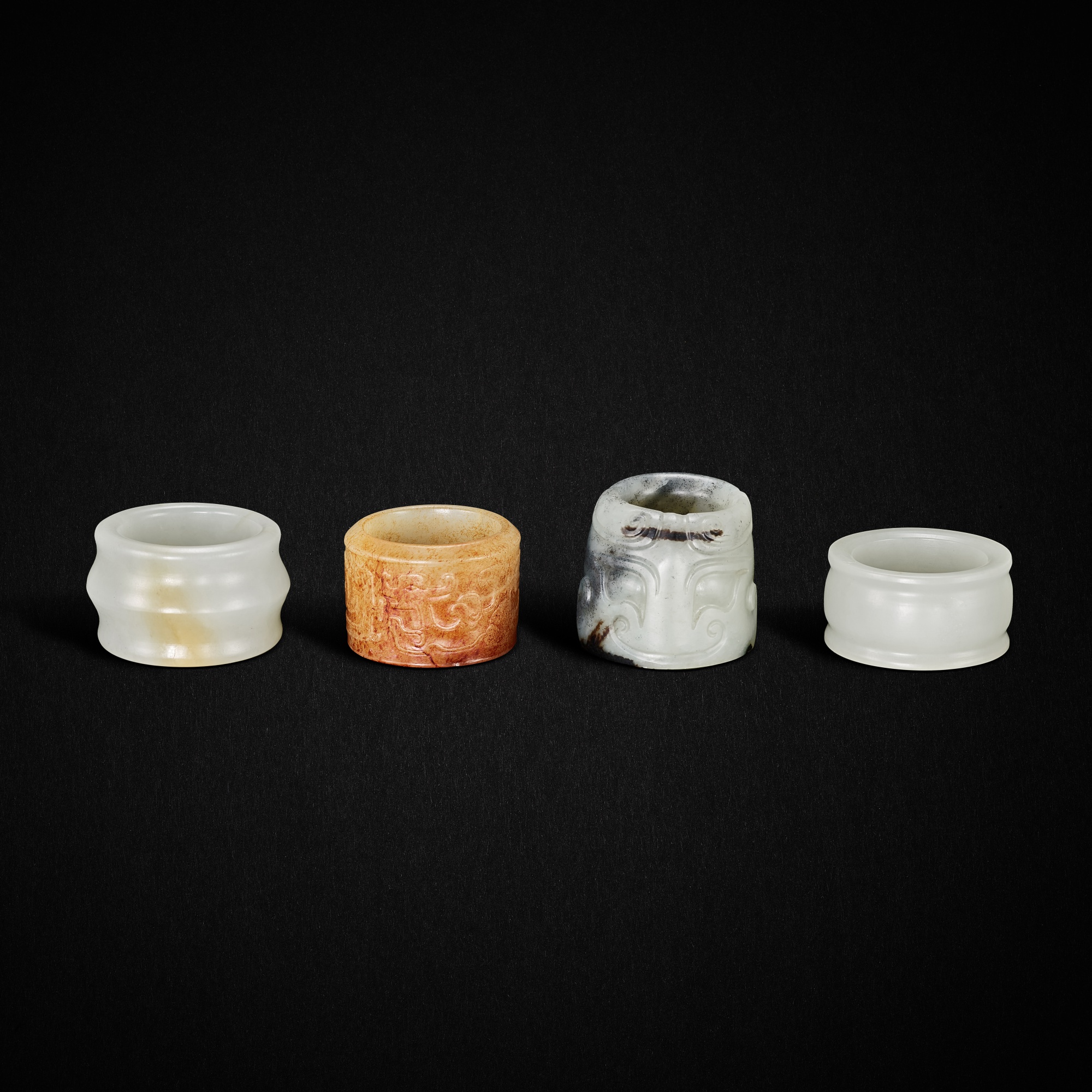 Three white and russet jade and a greyish-white jade thumb rings, Qing ...